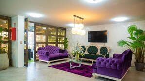 Uma sala de estar moderna com dois sofás roxos, uma mesa de centro de vidro e uma parede verde com lareira.