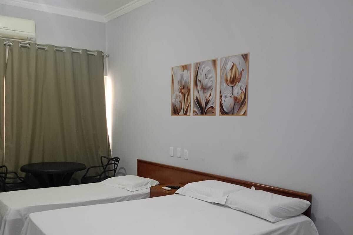 Quarto de hotel com duas camas, uma mesa, cadeiras, ar condicionado e obras de arte na parede.