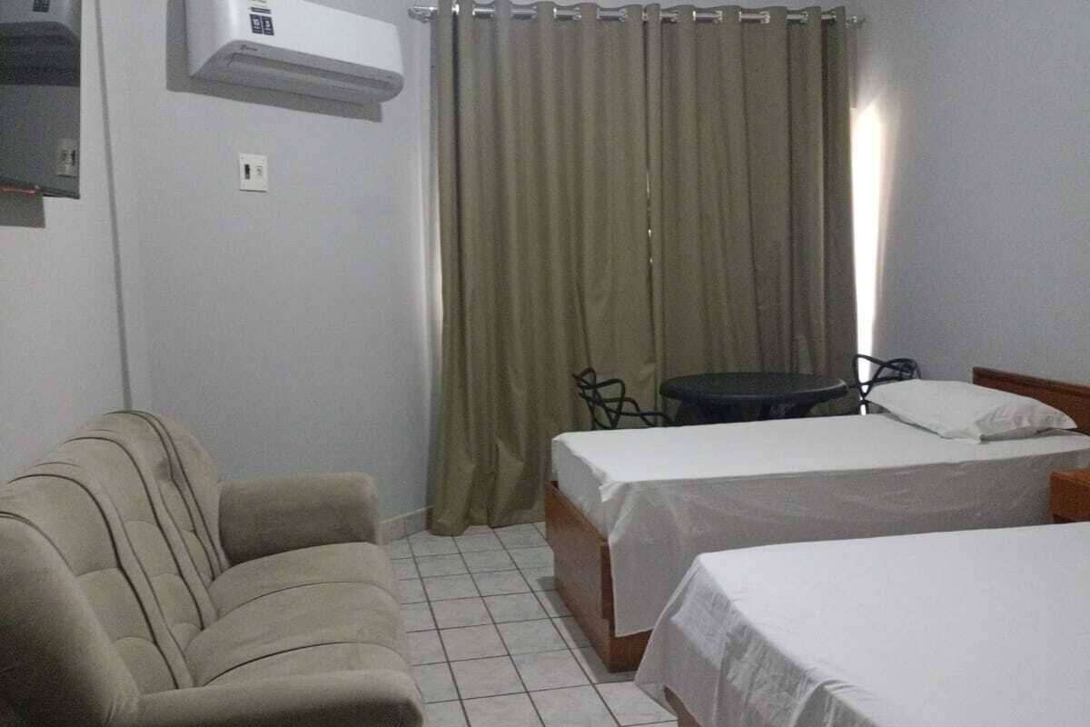 Quarto de hotel com duas camas, um sofá, uma escrivaninha e um aparelho de ar condicionado.