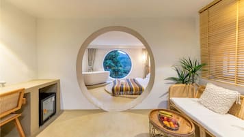 Quarto moderno com espelho redondo refletindo um banheiro, um sofá com uma cesta de frutas e uma pequena mesa.
