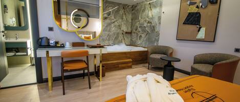 Quarto de hotel moderno com piso de madeira, uma escrivaninha com cadeira, um espelho grande, uma cama com cabeceira de madeira e um ar condicionado fixado na parede.
