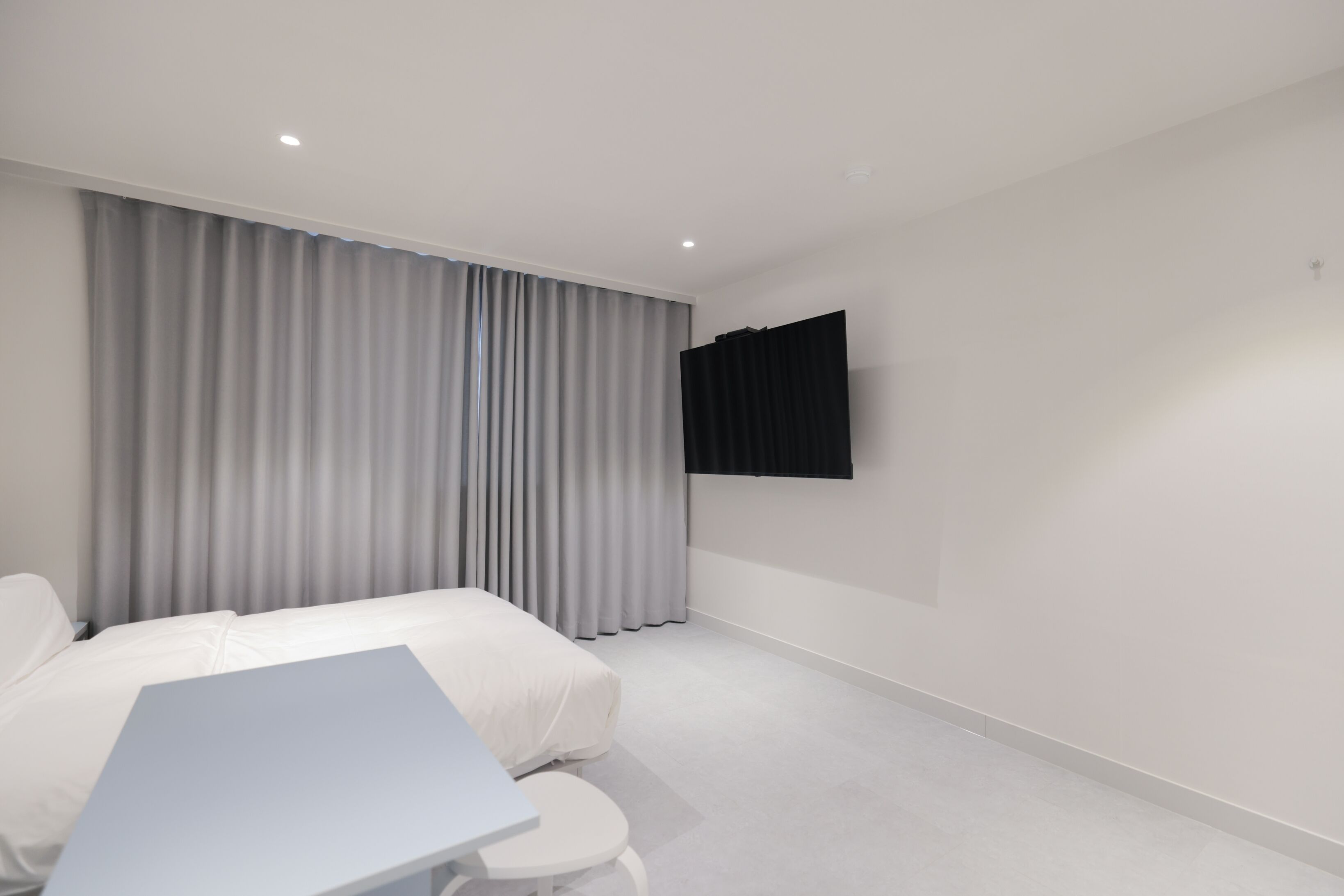 Quarto de hotel moderno com uma cama grande, uma mesinha e uma televisão na parede.