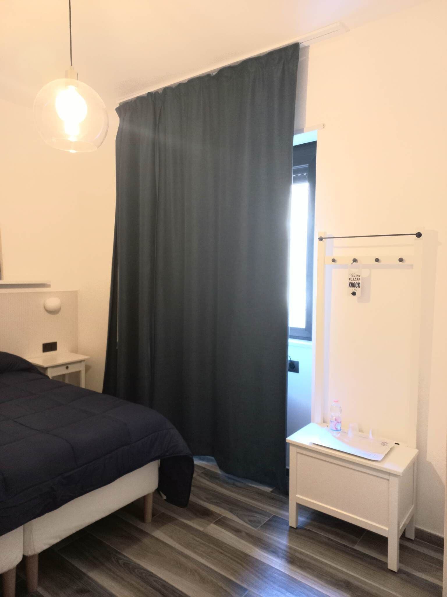 Quarto de hotel com cama, mesa de cabeceira, espelho e janela com cortinas.