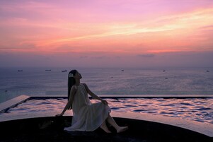 Uma mulher sentada à beira da piscina com vista para o pôr do sol.
