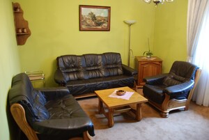 Uma sala de estar com sofá, poltronas, mesa de centro de madeira, abajur e um quadro na parede.