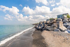 Uma praia com costa rochosa, um edifício com telhado plano e céu claro.