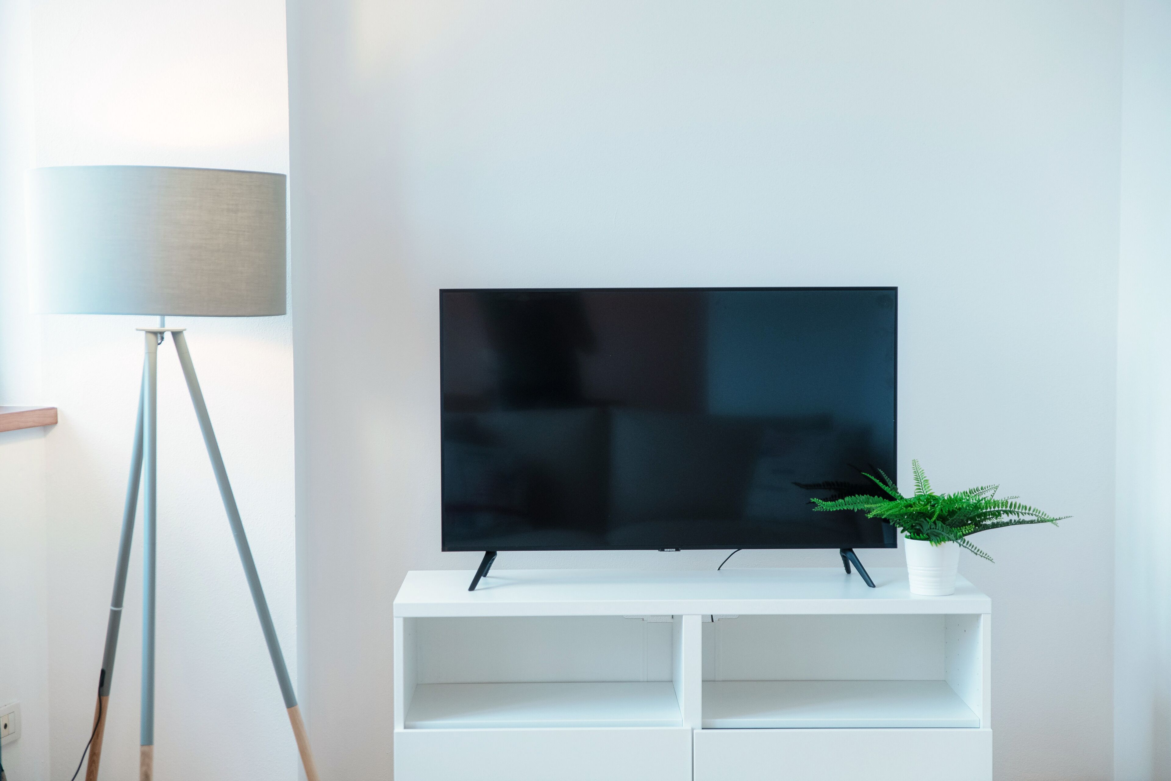 Uma unidade de entretenimento branca com uma televisão de tela plana, um abajur e um vaso com planta.