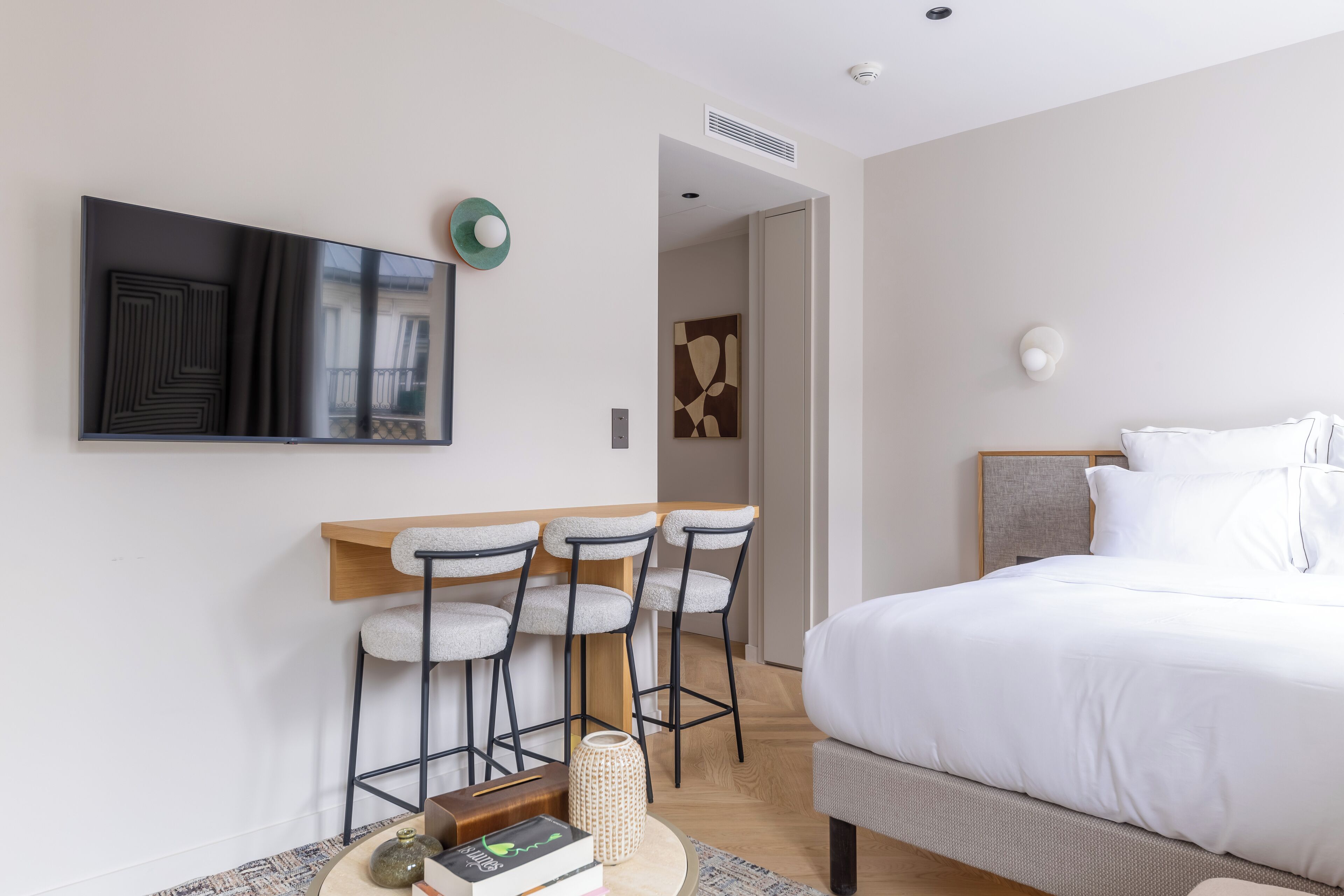 Quarto moderno com uma cama grande, uma TV fixada na parede e uma área de estar com banquetas.
