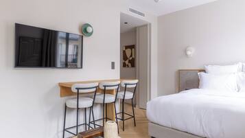 Quarto moderno com uma cama grande, uma TV fixada na parede e uma área de estar com banquetas.