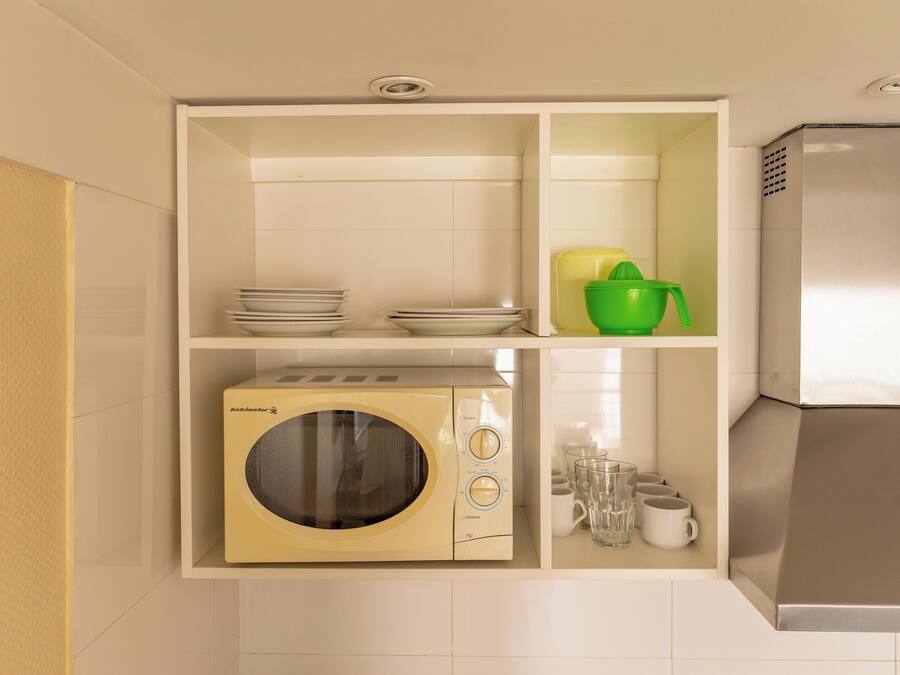 Uma cozinha compacta com micro-ondas, uma pia pequena e um exaustor de aço inoxidável.