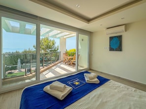 Quarto de hotel com uma grande porta de vidro deslizante que dá para um alpendre ao ar livre, uma cama com toalha azul e ar-condicionado fixado na parede.