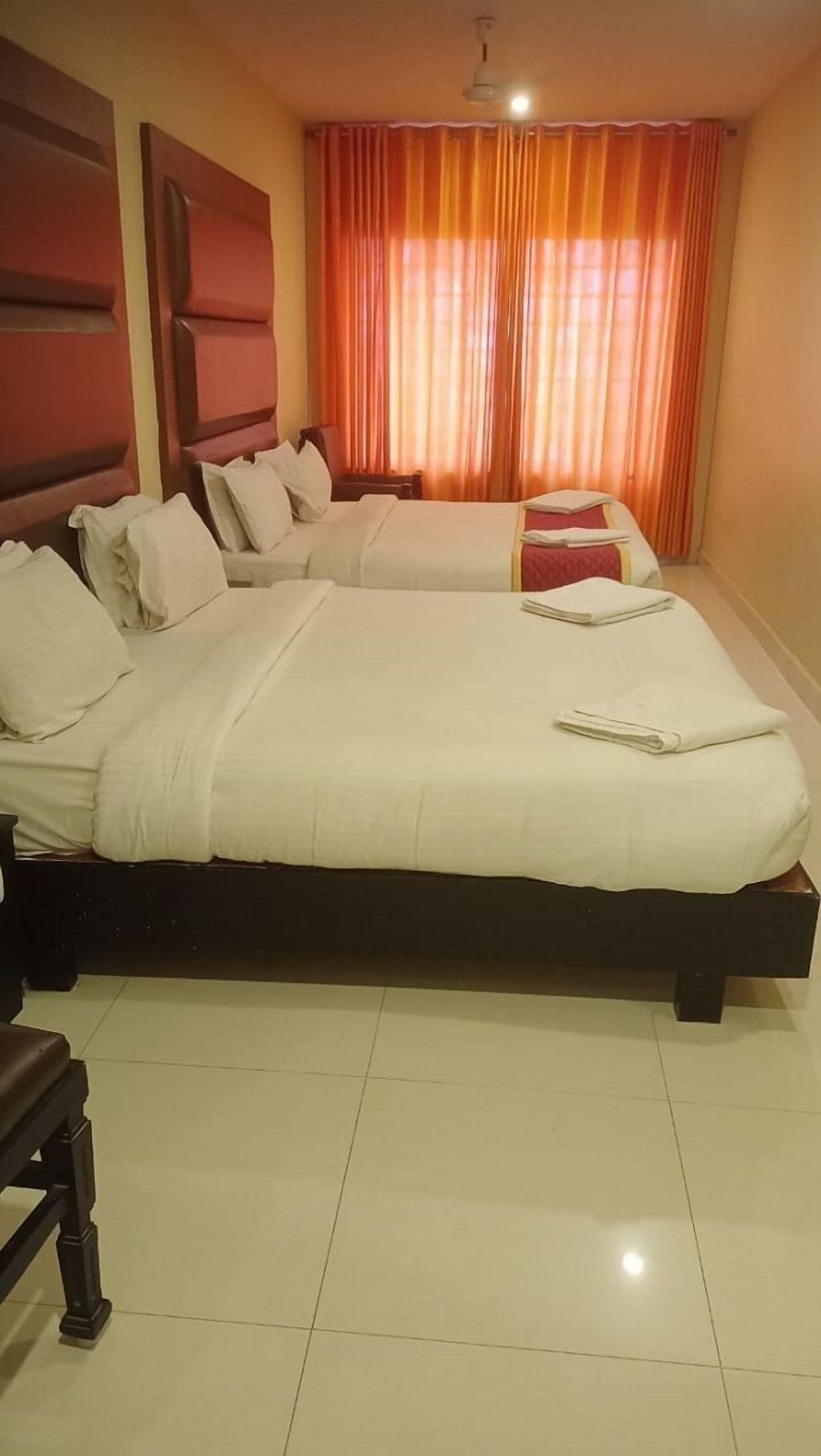 Quarto de hotel com duas camas, um espelho grande e cortinas laranja.