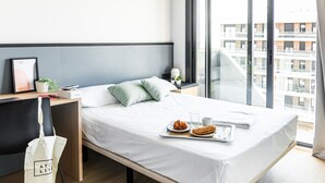 Quarto de hotel moderno com cama, escrivaninha e janela com vista para a cidade.