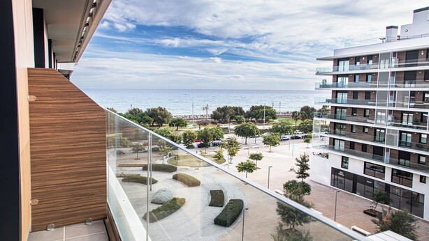 Apartamento moderno com varanda e vista para um pátio ajardinado e o mar.