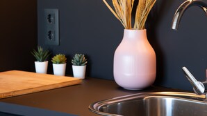 Cozinha com design moderno, apresentando uma pia de aço inoxidável, um vaso rosa com plantas secas e um micro-ondas sobre o balcão.