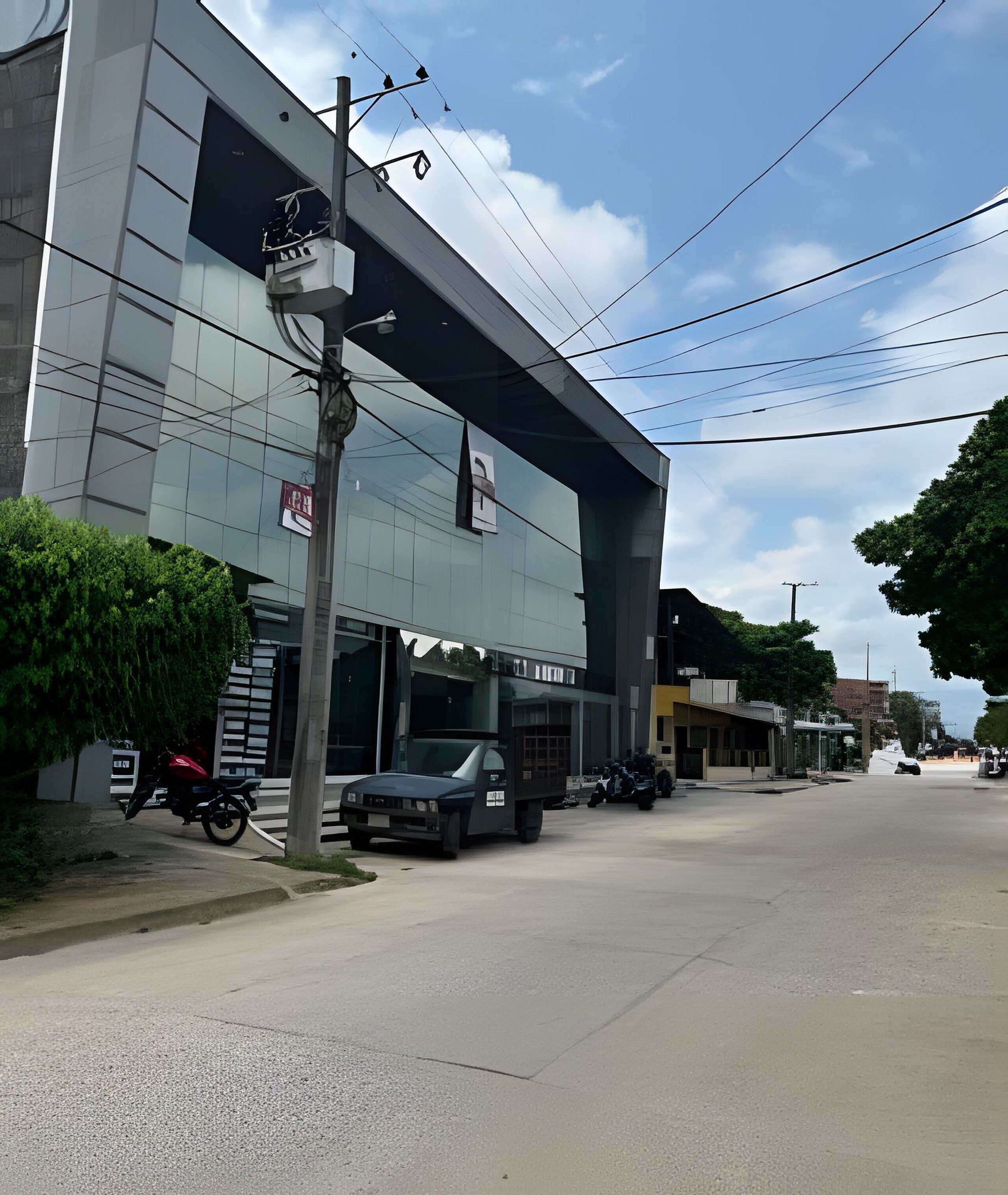 Um edifício moderno com fachada de vidro ampla, um caminhão estacionado em frente e uma motocicleta na calçada.