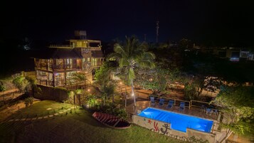 Um edifício de vários andares com área de piscina, cercado por vegetação exuberante e palmeiras.