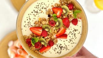 Uma taça de iogurte coberta com granola, morangos, kiwi e sementes de chia.