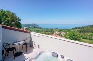 Uma varanda com hidromassagem, duas cadeiras e vista para o mar e vegetação.