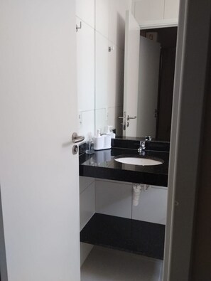 Uma casa de banho com uma pia branca, um espelho e uma porta que dá para outro espaço.