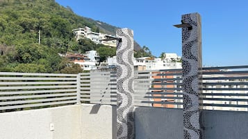 Um deck de madeira com um pilar e guarda-corpo decorados, com vista para uma encosta onde se veem edifícios.
