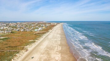 Uma cidade costeira com uma extensa praia de areia, vista clara do oceano e uma combinação de edifícios residenciais e comerciais.