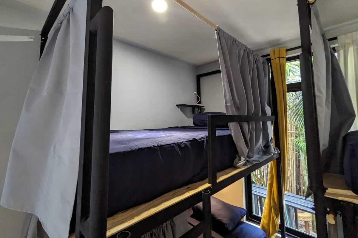 Quarto com beliche, janela, mesa pequena e cortina.