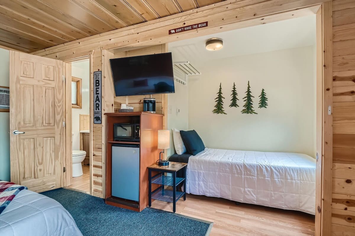 Um quarto de cabana aconchegante, com uma cama, uma TV, um micro-ondas e uma pequena mesa.