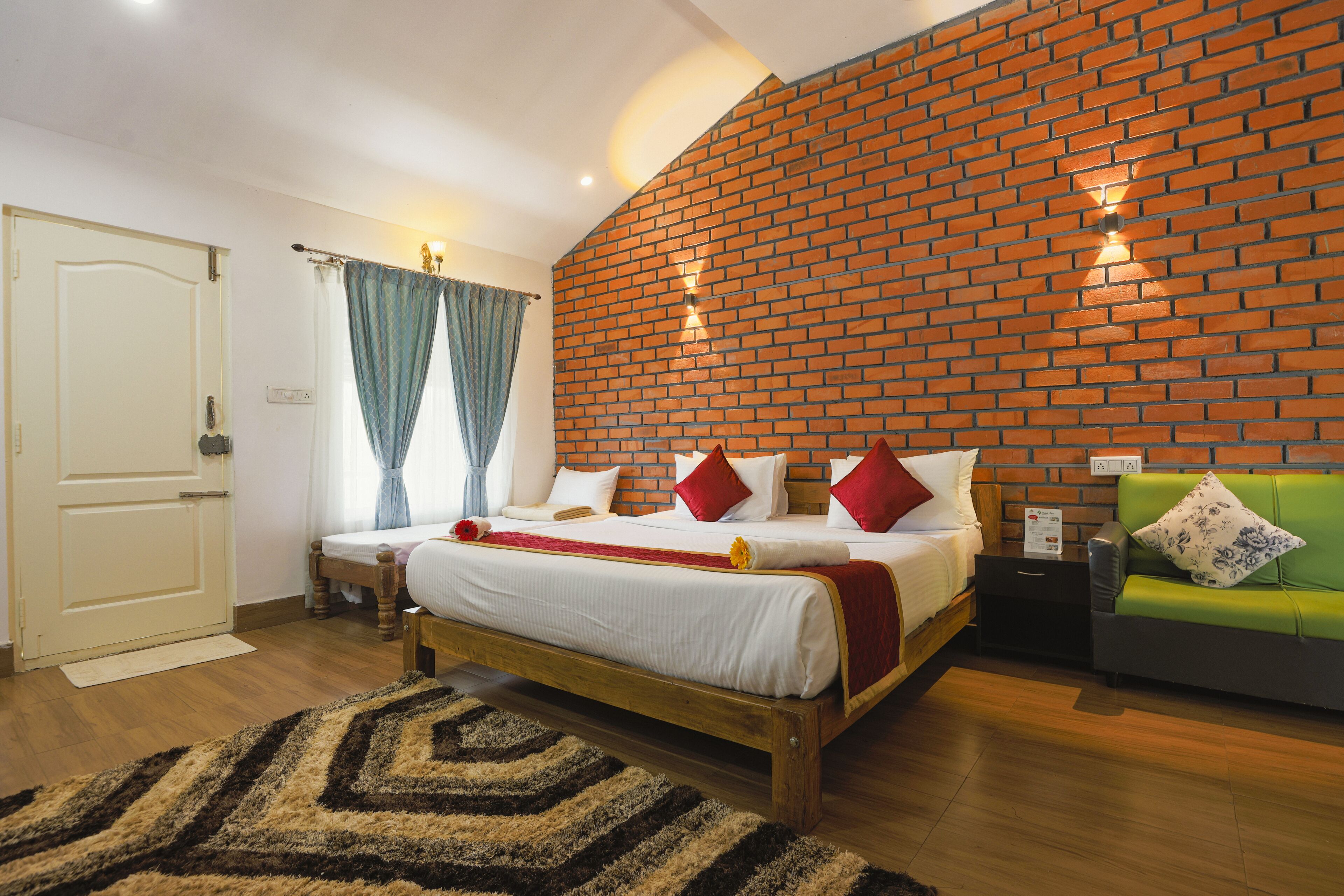 Quarto com parede de tijolos, cama de madeira, sofá verde e mesa de cabeceira com abajur.
