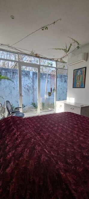 Quarto com uma cama grande, uma escrivaninha e uma cadeira. Há uma janela com vista para o exterior.
