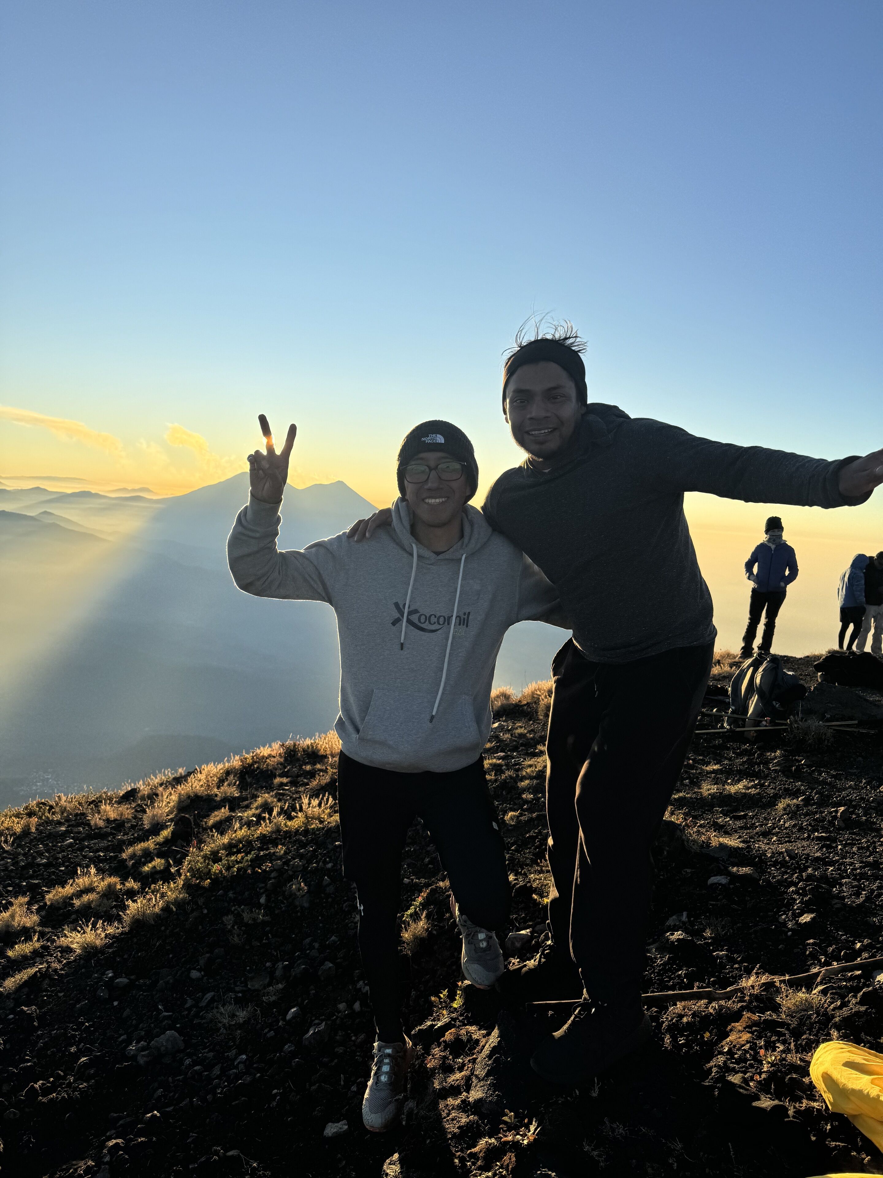 Duas pessoas no cume de uma montanha, com céu limpo e montanhas ao longe.
