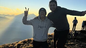 Duas pessoas no cume de uma montanha, com céu limpo e montanhas ao longe.