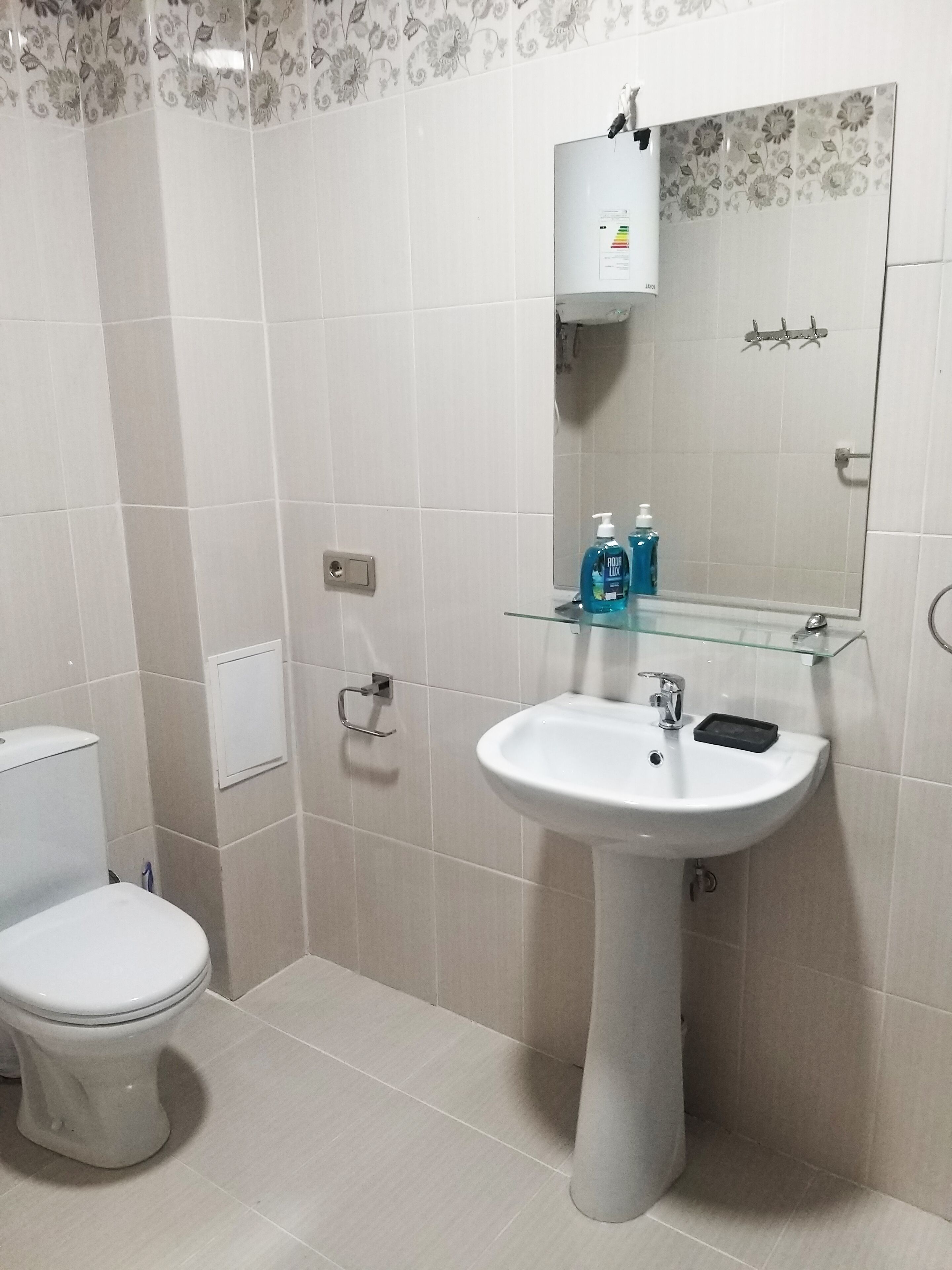 Uma casa de banho com sanita, lavatório sobreposta e uma prateleira de vidro com produtos de higiene pessoal, além de um espelho.