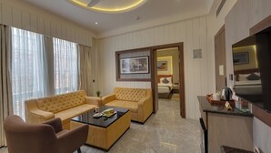 Quarto de hotel moderno com sofá, mesa de centro, televisão e cama com mesa de cabeceira.
