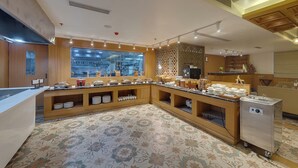 Uma área de buffet com diversas opções de comida, uma máquina de café e uma geladeira.