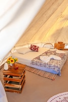 Acolhimento em tenda confortável, com cama, almofadas, uma pequena mesa de madeira com um vaso de flores e um tapete.