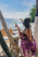 Uma pessoa sentada numa cadeira de praia à beira-mar, segurando uma bebida.
