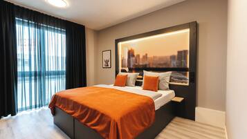 Quarto de hotel moderno com uma cama grande, vista da cidade pela janela e uma pintura urbana na parede.