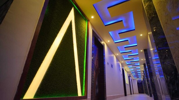 Um corredor com design moderno, apresentando um luminário geométrico no teto e uma parede texturizada à esquerda.