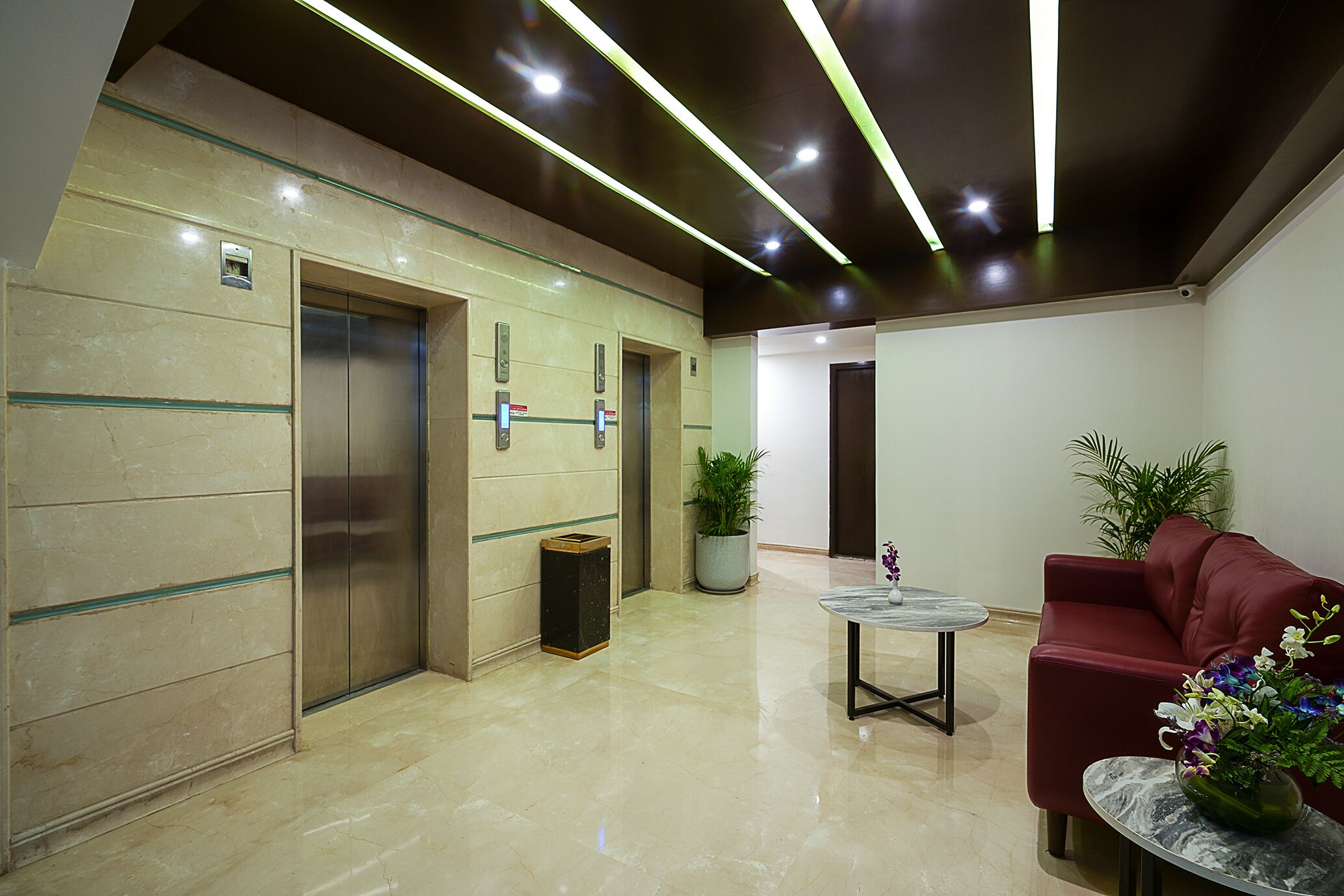 Um hall moderno com piso de mármore, um sofá vermelho, uma mesinha de centro de mármore, uma planta em vaso e um elevador.