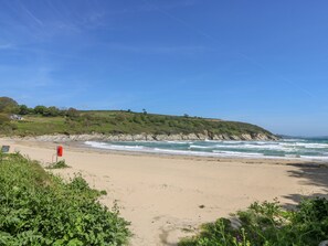 Uma praia com ondas, uma bandeira vermelha de salva-vidas e vegetação.