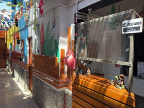 Um banco de madeira com estrutura de vidro, um mural colorido e um sinal com a senha do Wi-Fi.