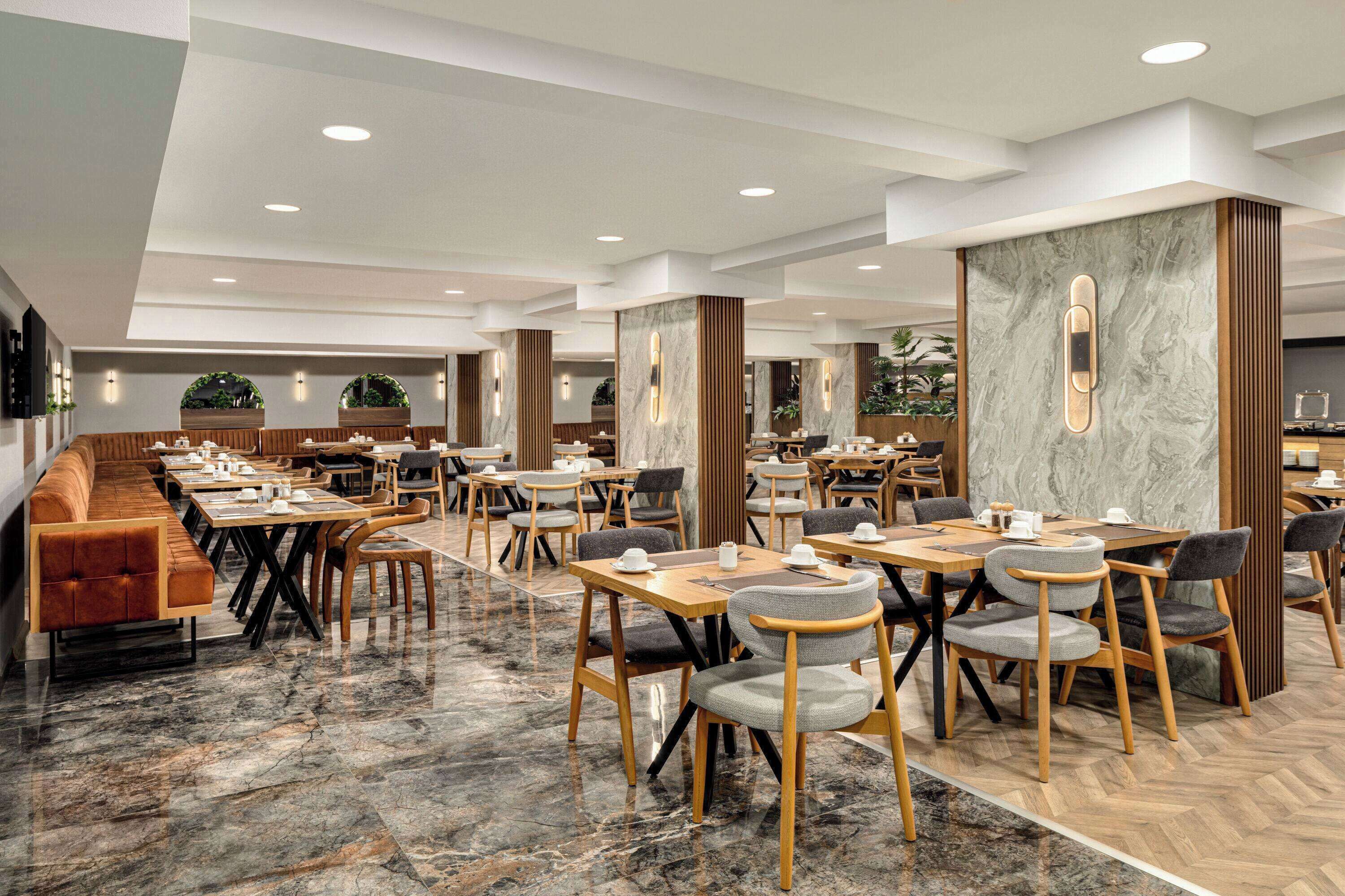 Restaurante moderno com mesas comunitárias alongadas e cabines, piso de mármore e detalhes em madeira.