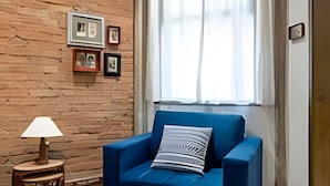 Um quarto com um sofá azul, uma mesa pequena, uma luminária e uma janela com cortinas.