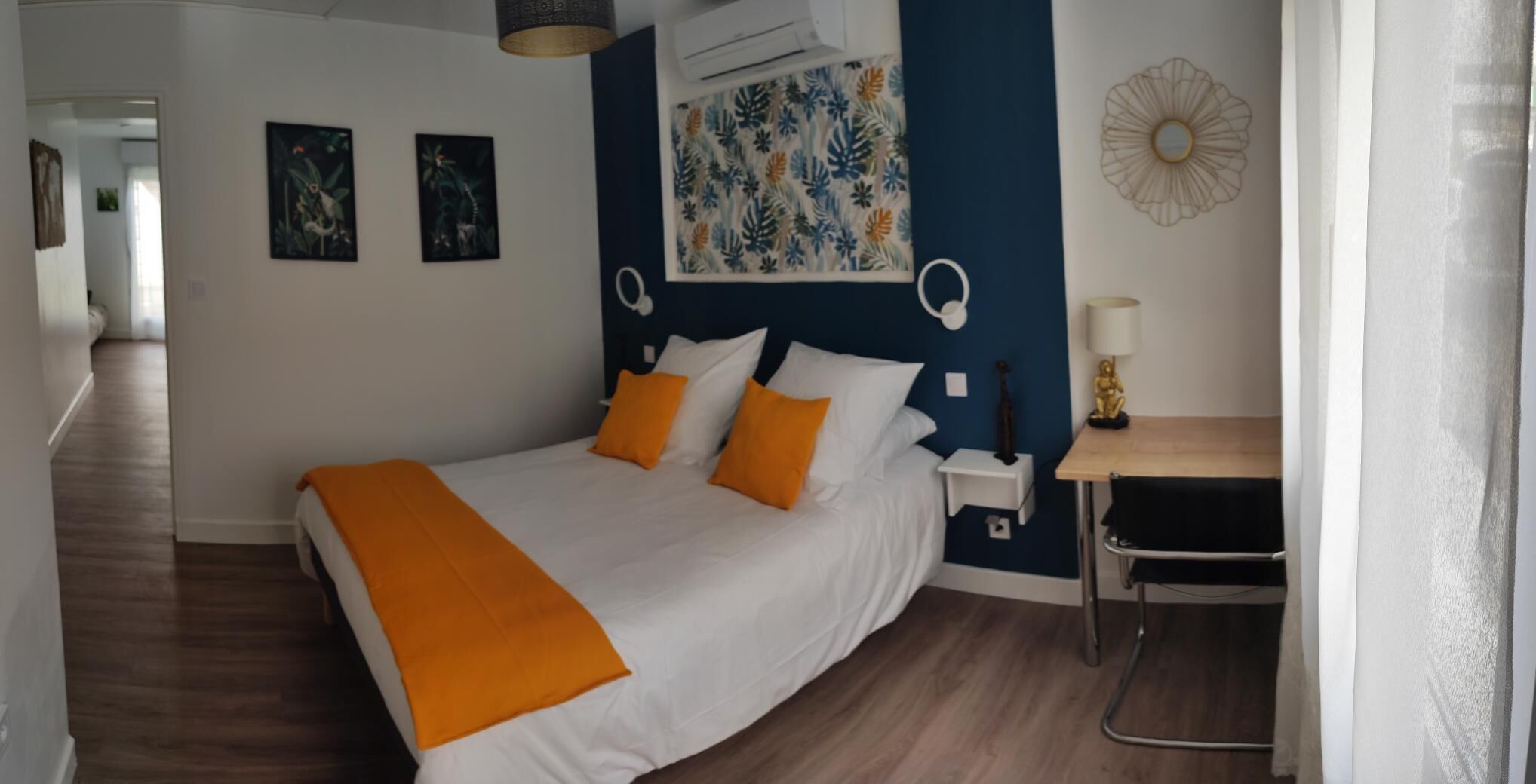 Quarto com cama, escrivaninha e cadeira. Há obras de arte nas paredes e um enfeite decorativo.