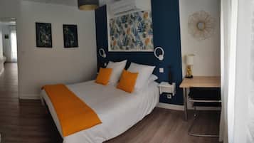 Quarto com cama, escrivaninha e cadeira. Há obras de arte nas paredes e um enfeite decorativo.