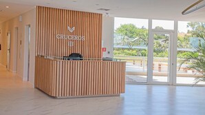 Balcão de recepção com design em painel de madeira e um logotipo, divisória de vidro e vista para o verde lá fora.