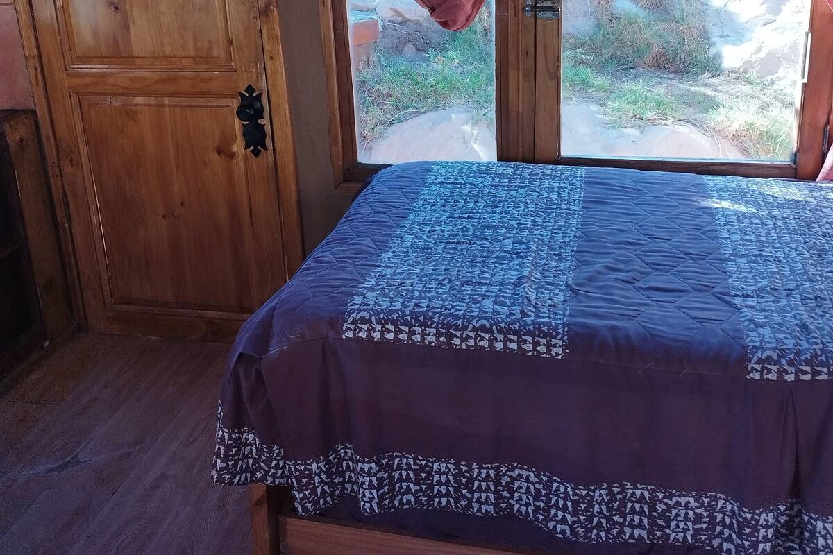 Um quarto com porta de madeira, janela com cortinas vermelhas e cama com colcha estampada.