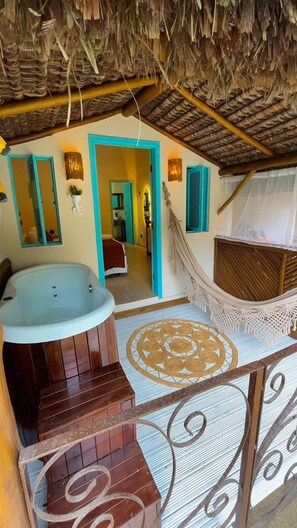 Um quarto acolhedor com telhado de colmo, uma banheira grande e uma rede.