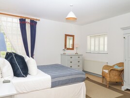 Um quarto com cama, cômoda, cadeira, janela com persianas e luminária pendente.
